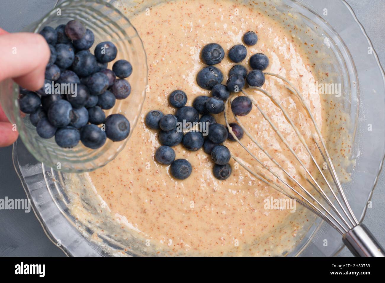Top view of crop anonymous person with whisk pouring blueberries into ...
