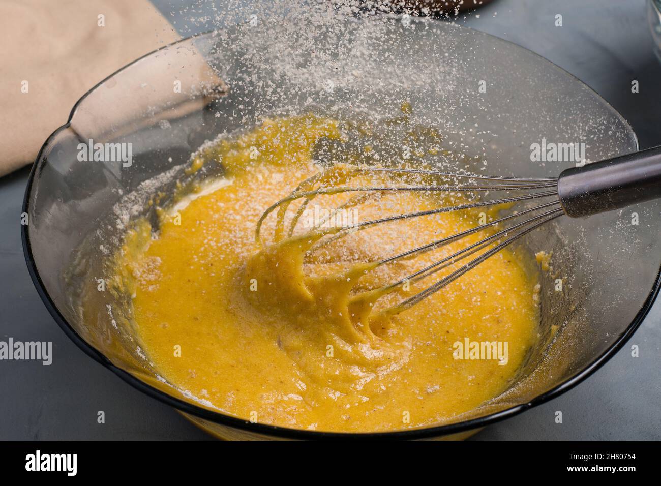 Flour pouring into glass bowl with raw whipped egg yolk and whisk ...