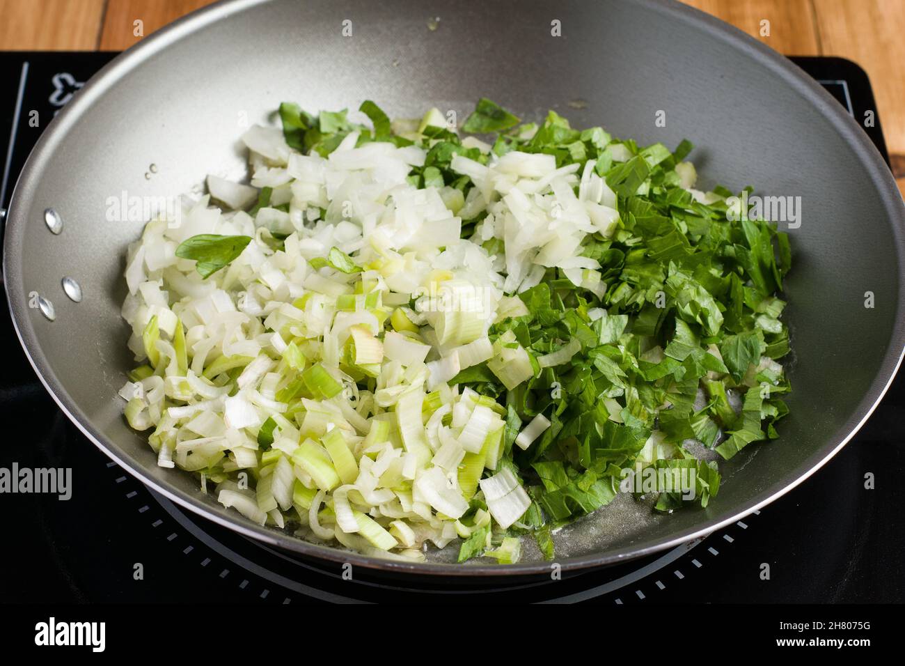 Fresh chopped green onion frying in metal pan on modern black cooker ...