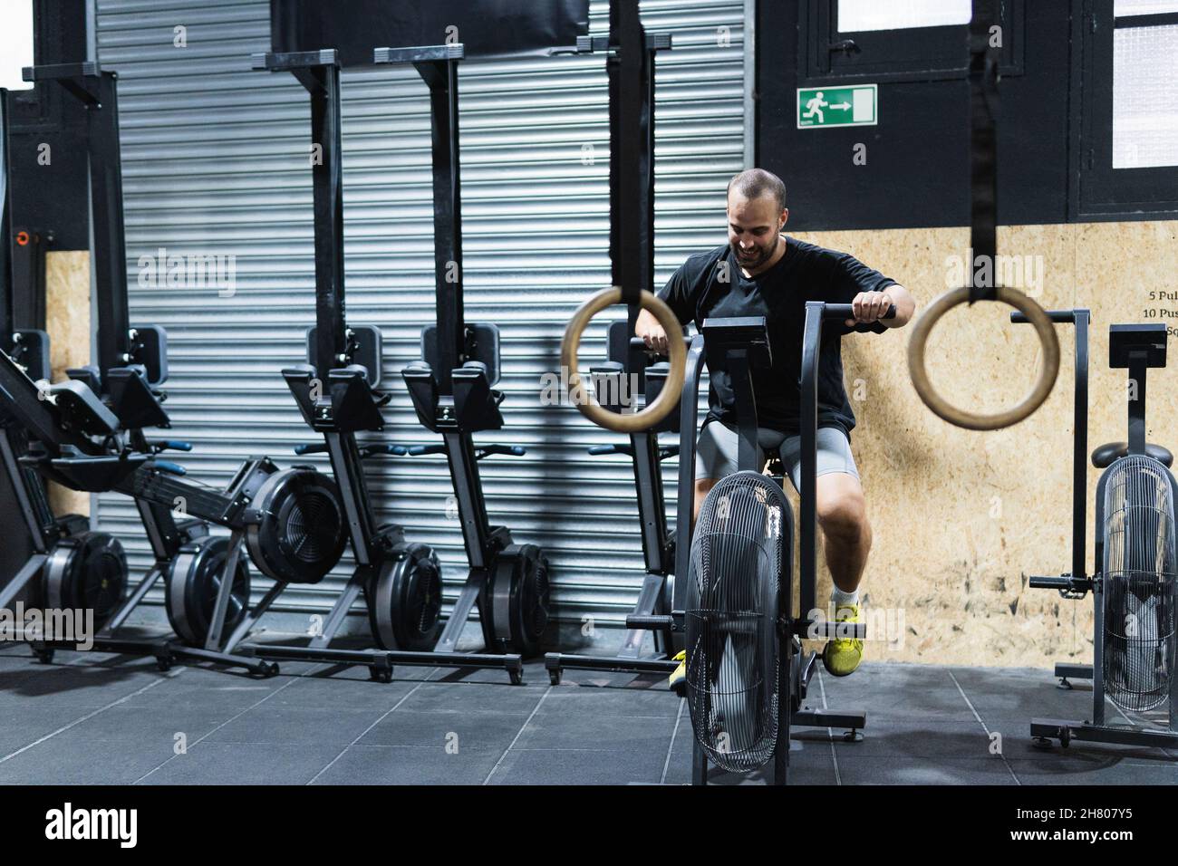 Full body of focused male exercising on air bike during intense ...