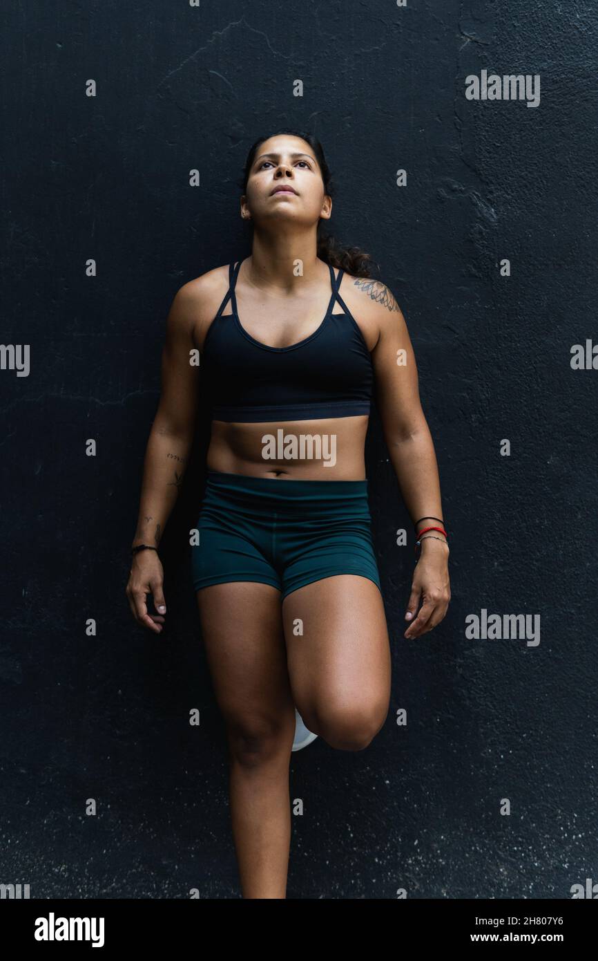 Serious Hispanic sportive female in activewear looking up with crossed ...