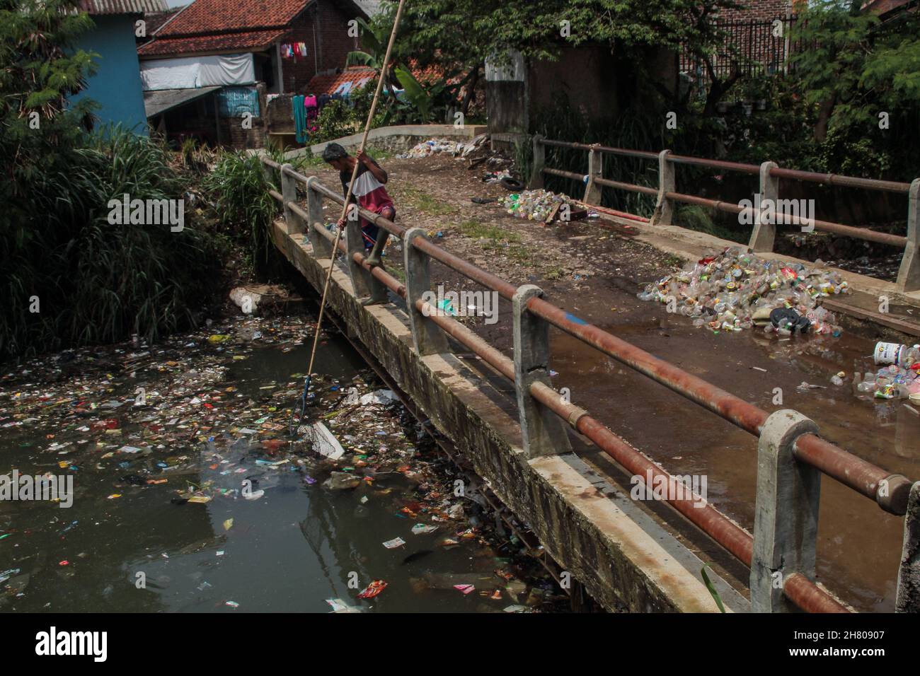 A man nets plastic waste to let water flow in the Bojong Citepus River ...