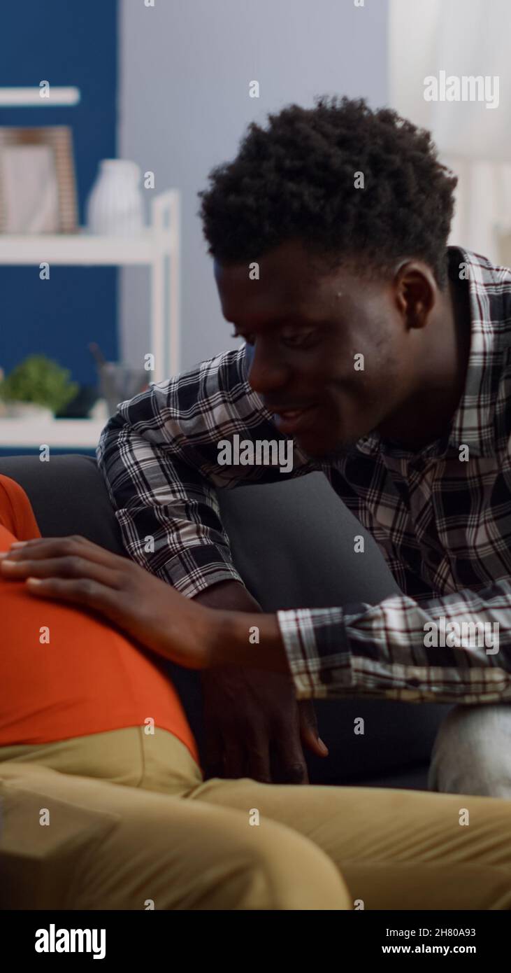 Pregnant interracial couple sitting on living room couch. African ...