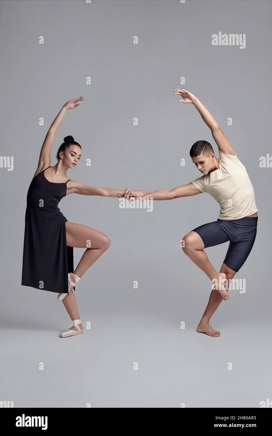 Two athletic modern ballet dancers are posing against a gray studio ...