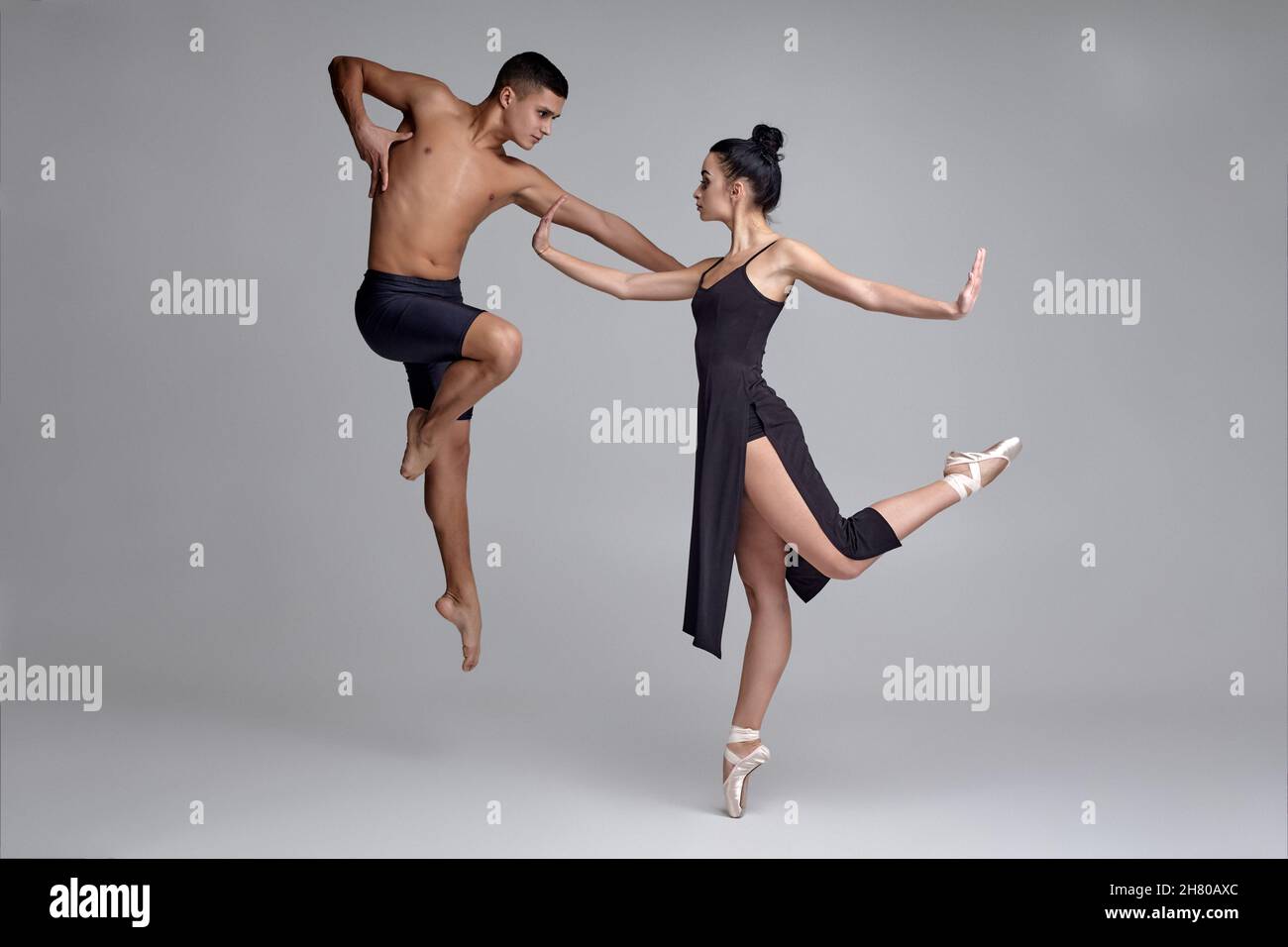 Two athletic modern ballet dancers are posing against a gray studio ...