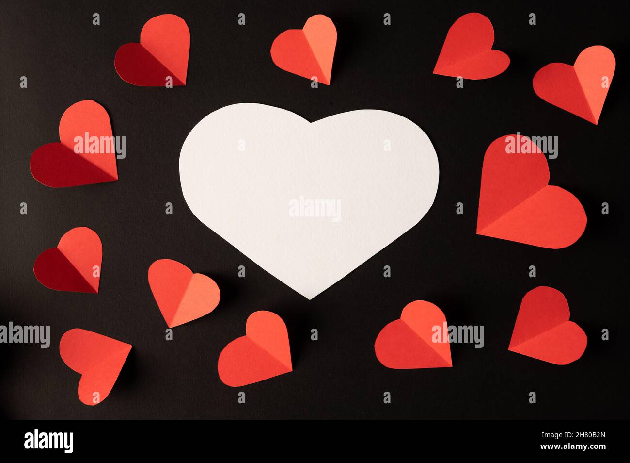 White hearts and red hearts made of paper are placed on a black ...