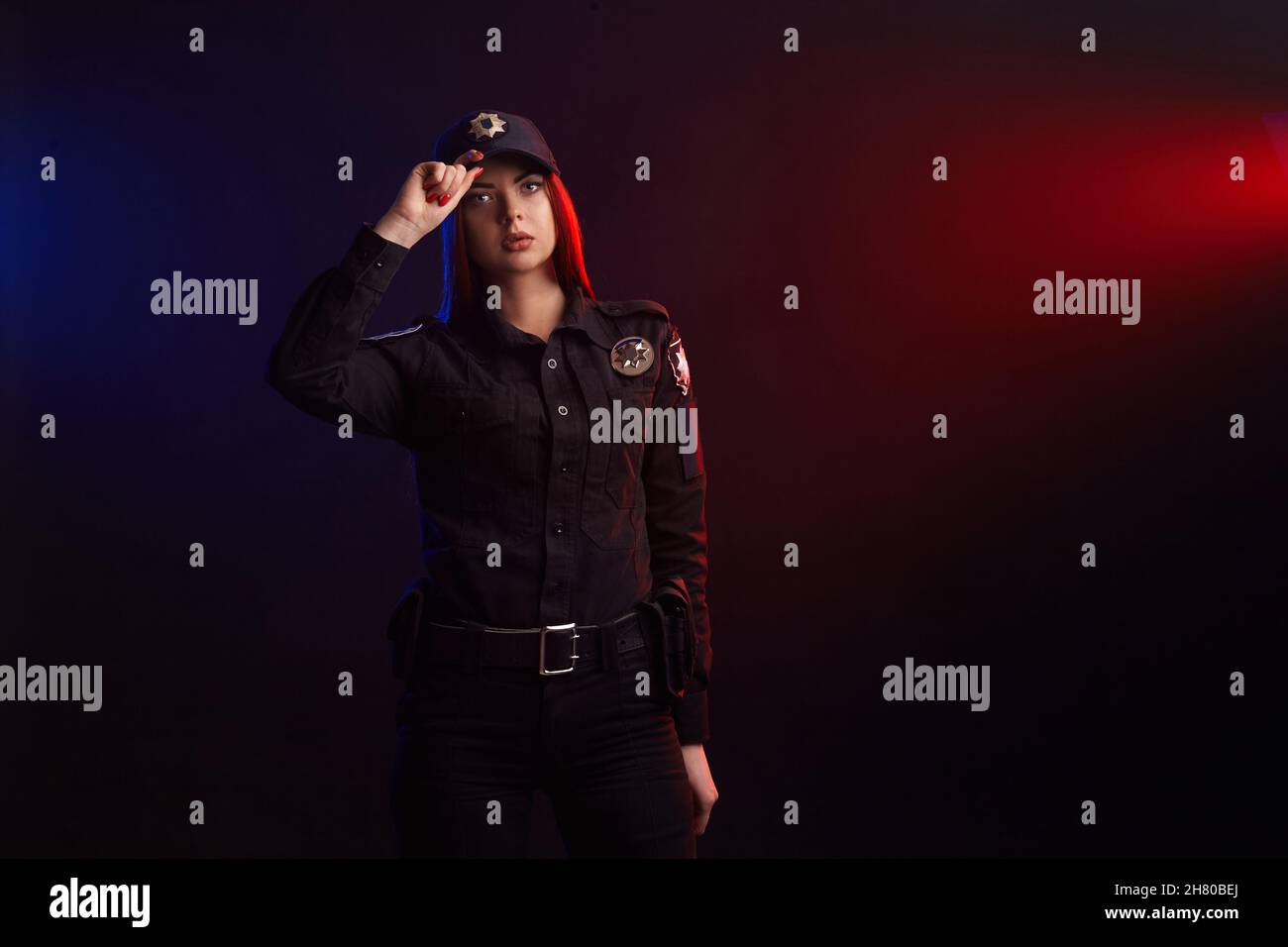 Serious female police officer is posing for the camera against a black ...