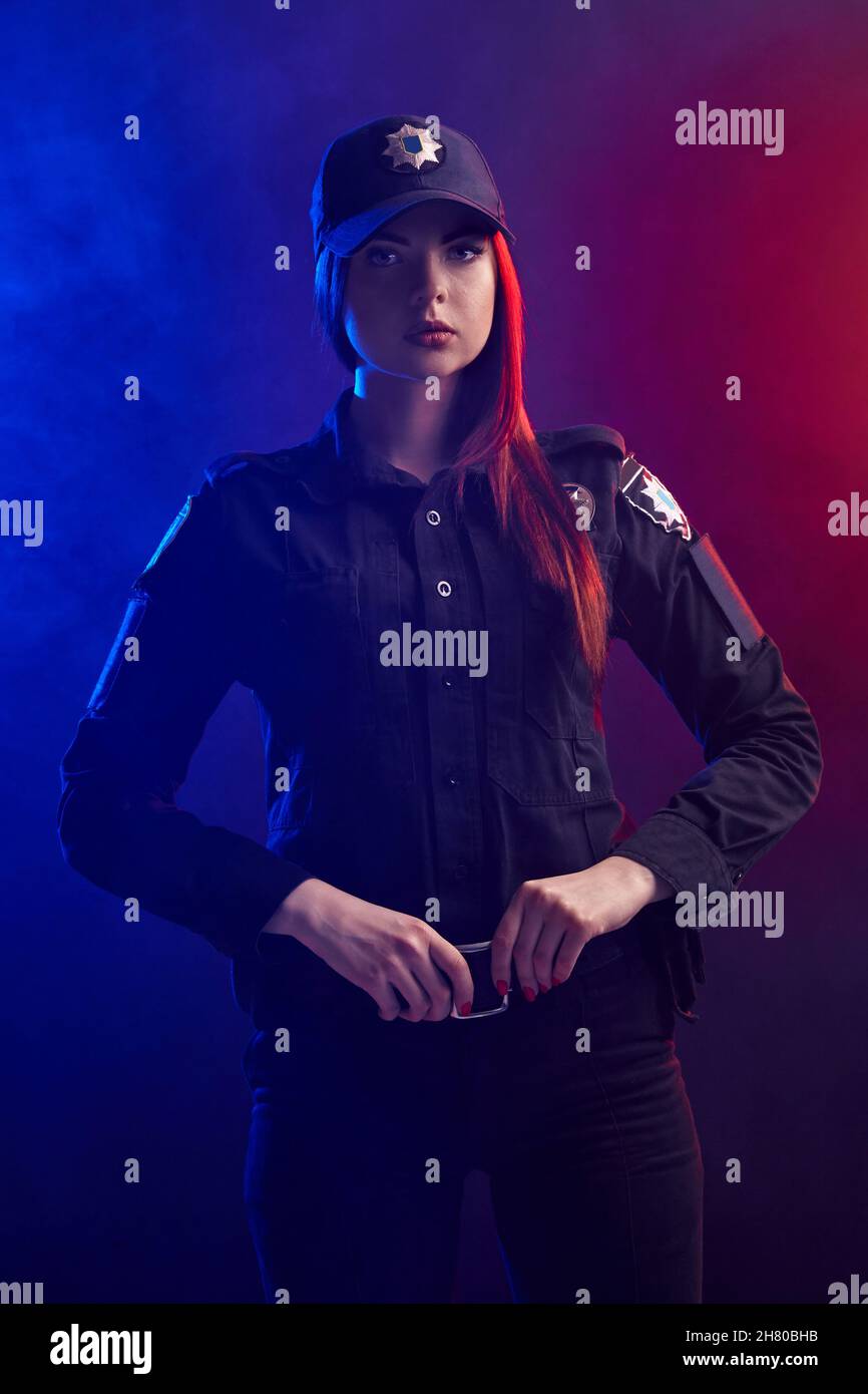 Serious female police officer is posing for the camera against a black ...