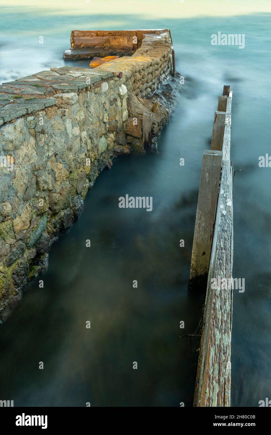old sea wall wooden breakwater or groyne with glassy water on the ...