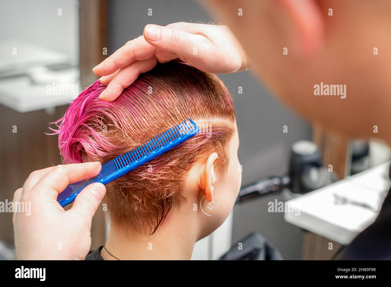 Combing the hair of a young woman during coloring hair in pink color at ...