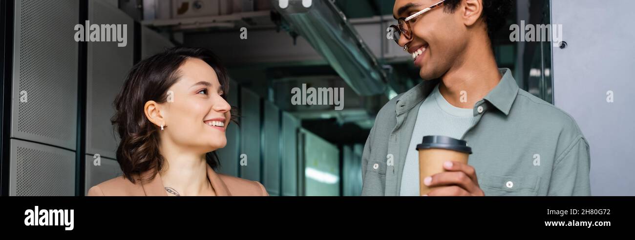 african american administrator with coffee to go smiling near colleague ...