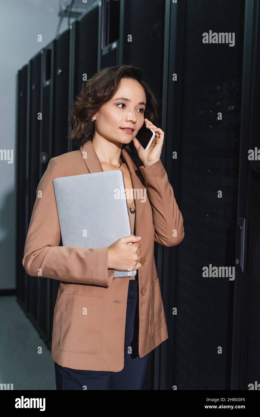technician with laptop talking on mobile phone while working in data ...