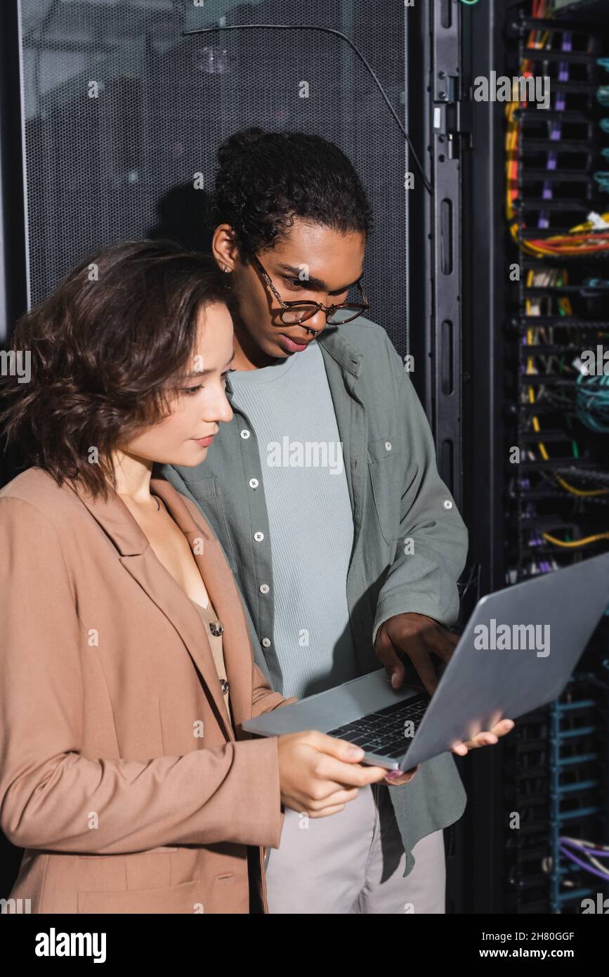 couple of multiethnic engineers looking at laptop while checking server ...