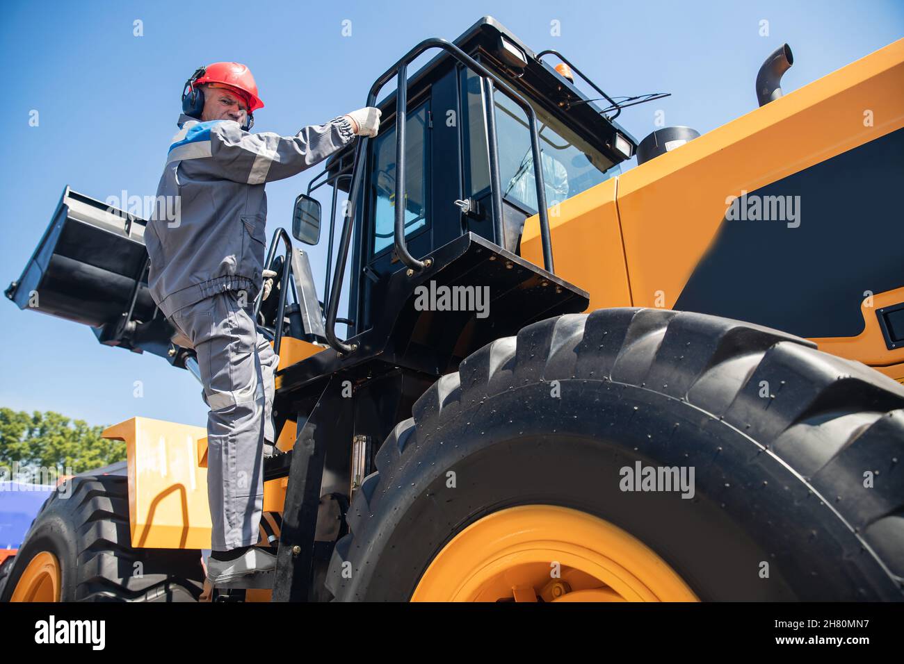 Industrial portrait of working man, excavator driver climbs into cab to ...