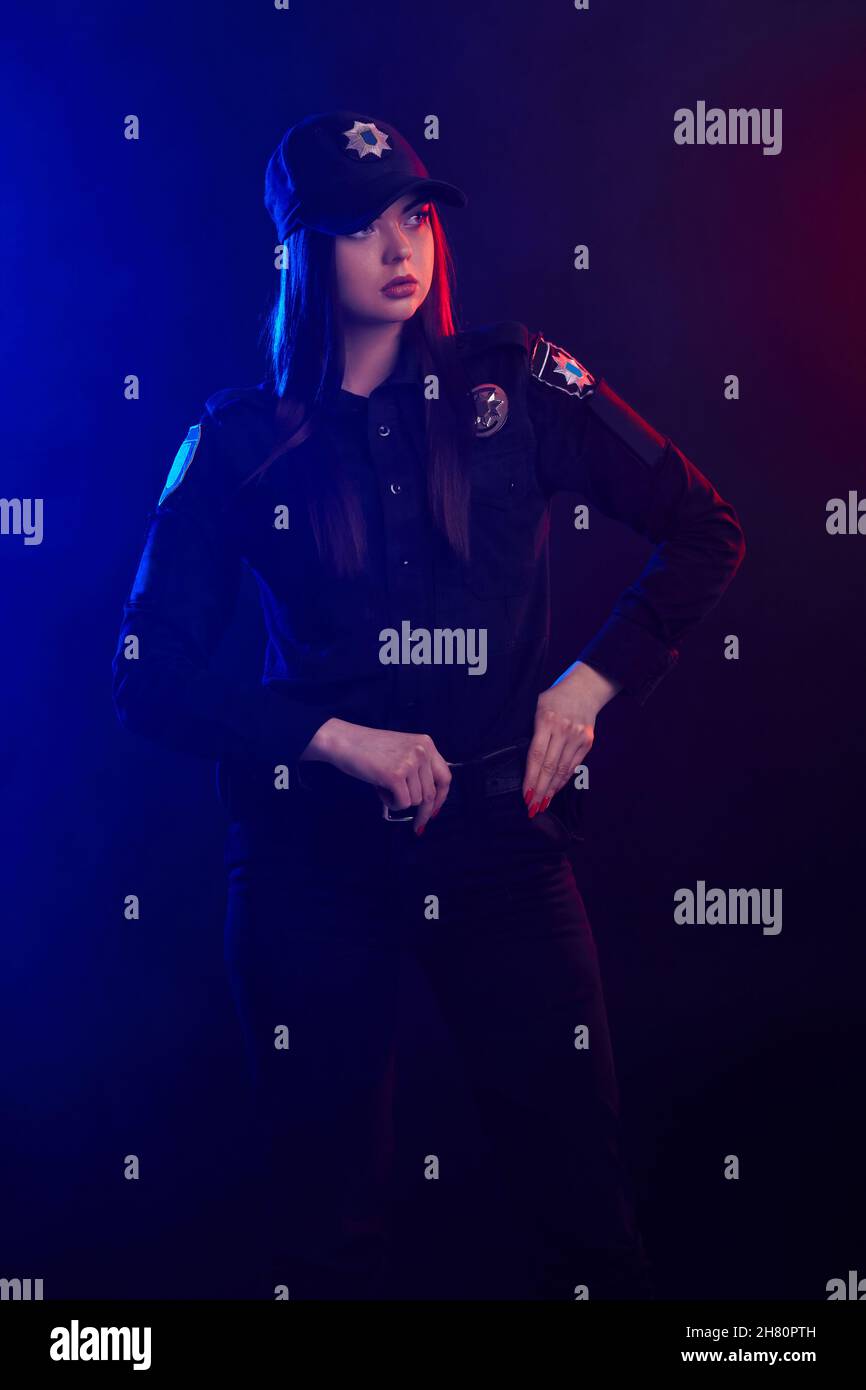 Serious female police officer is posing for the camera against a black ...