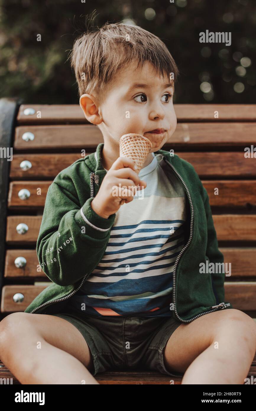 Portrait of a caucasian little boy eating ice cream while sitting on a ...
