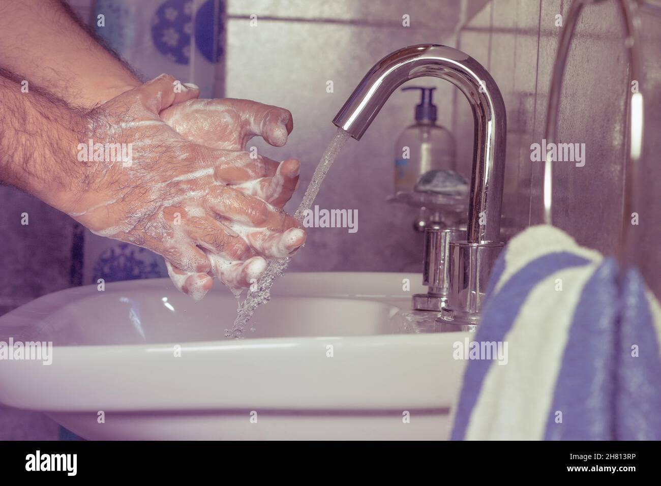 Side view of a man washing his hands with soap under the steel faucet ...