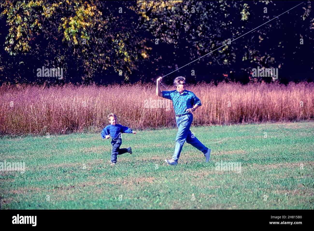 A father and son run across a field pulling a kite string to get the ...