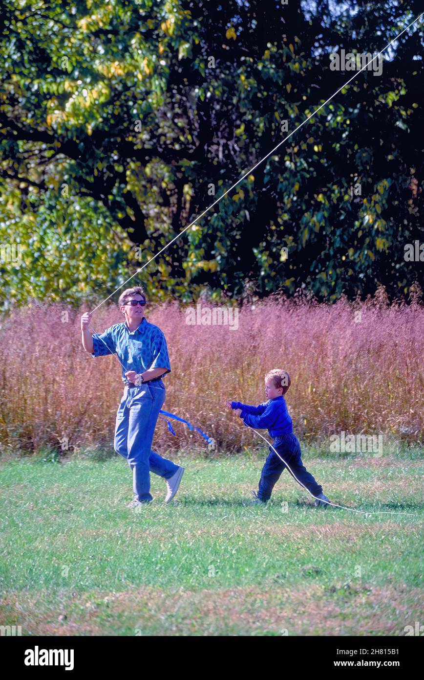 A father and son run across a field pulling a kite string to get the ...