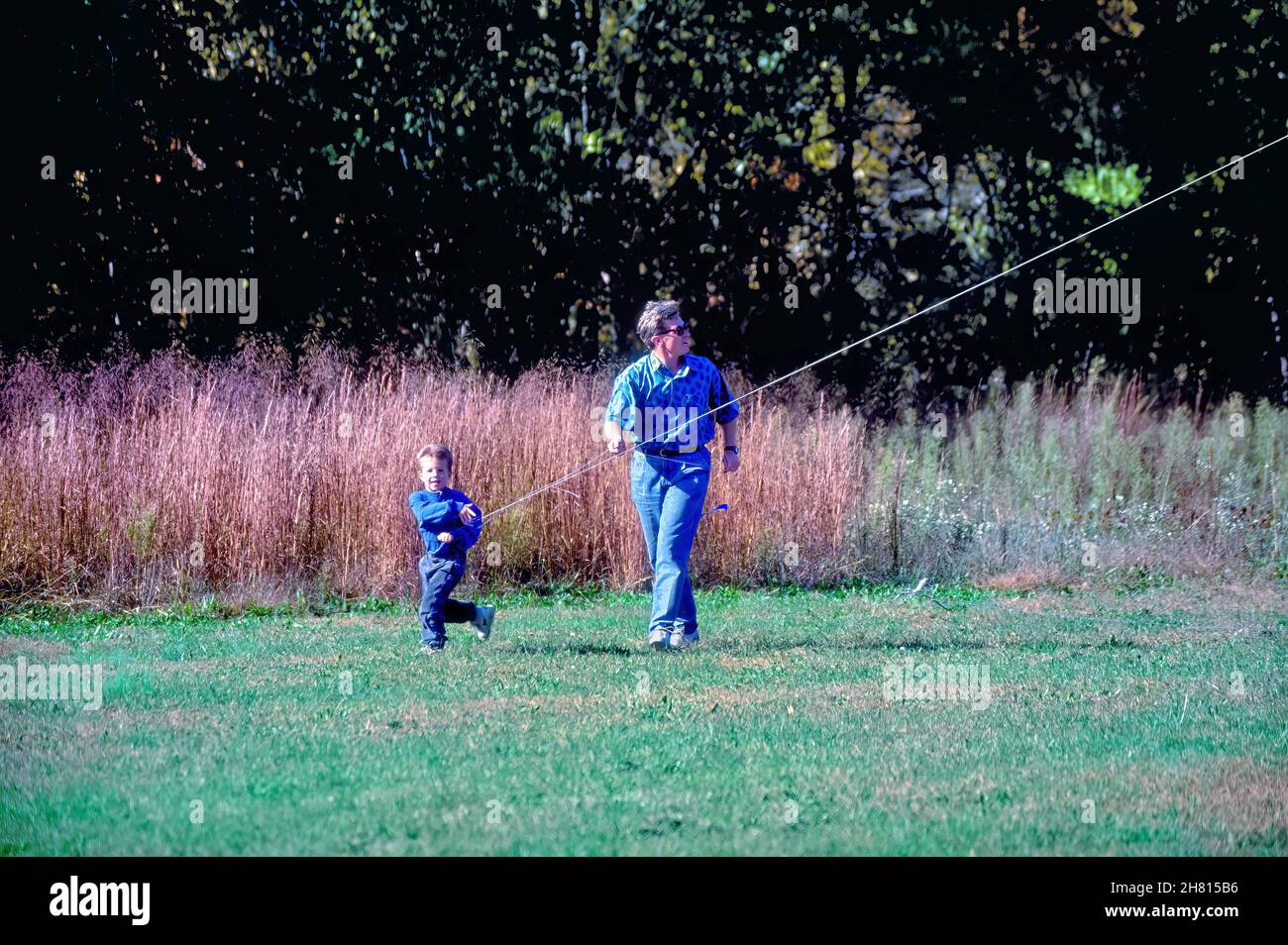 A father and son run across a field pulling a kite string to get the ...