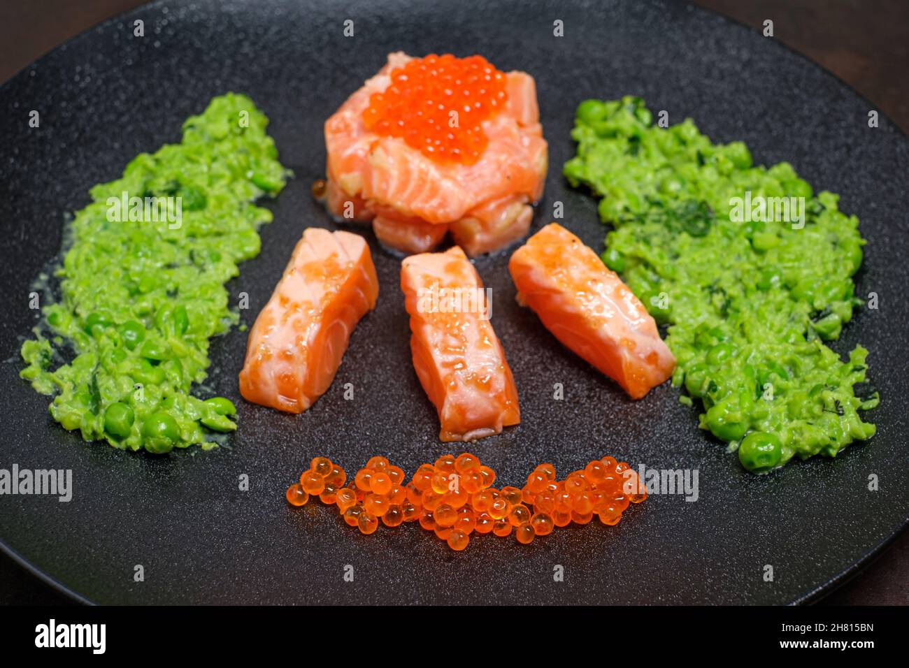 Salmon with orange caviar and mashed peas on a black plate Stock Photo ...