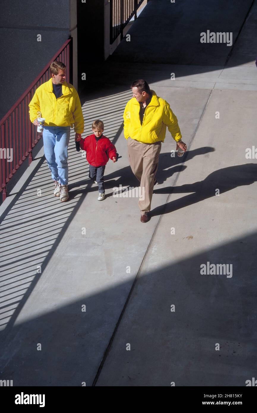 Two men walk with a small boy on a sun-drenched walkway at a football ...