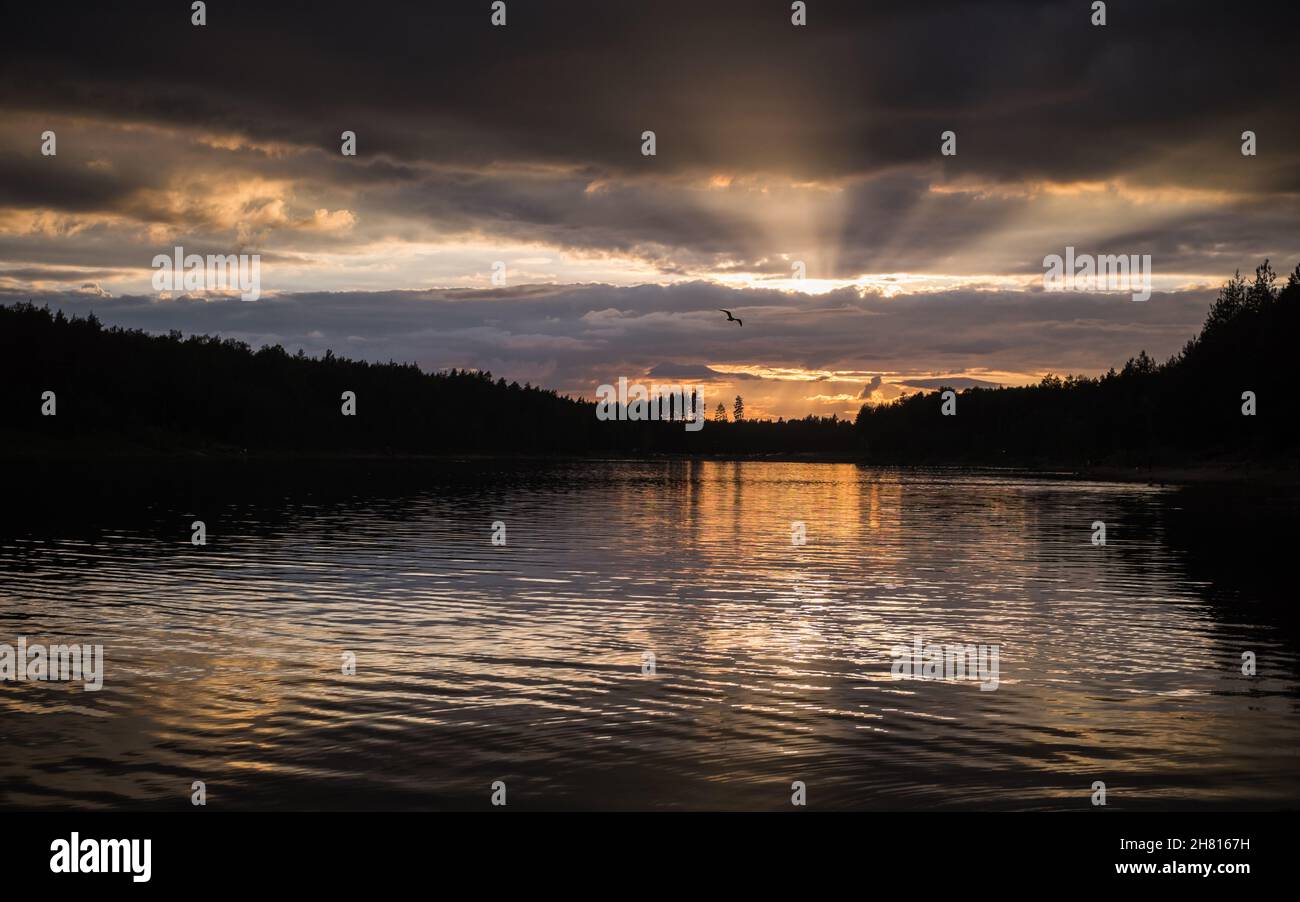 A sunset scene on a forest lake with sun rays breaking through dark ...