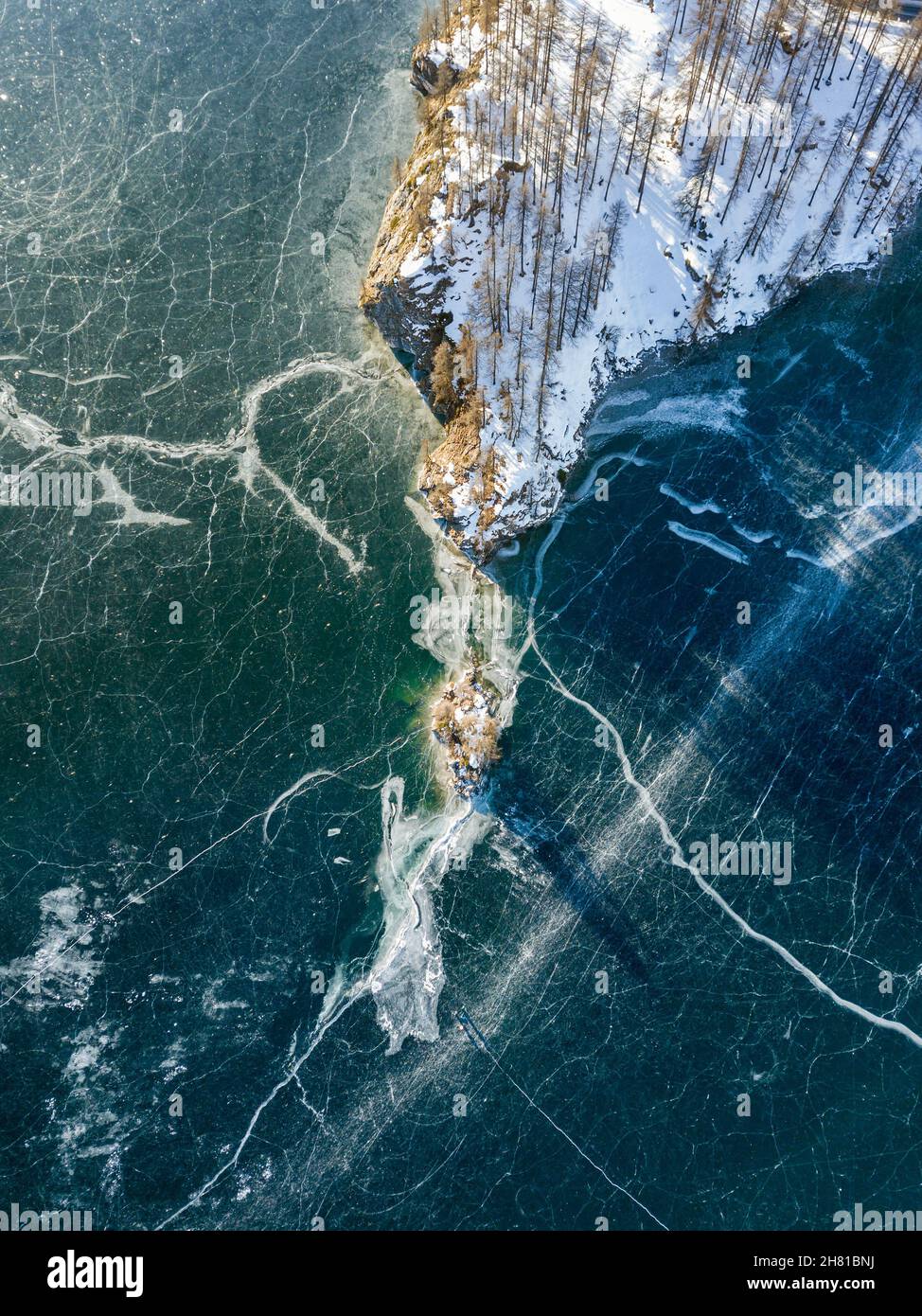 Aerial view of an island tip on a frozen lake with many ice cracks on ...