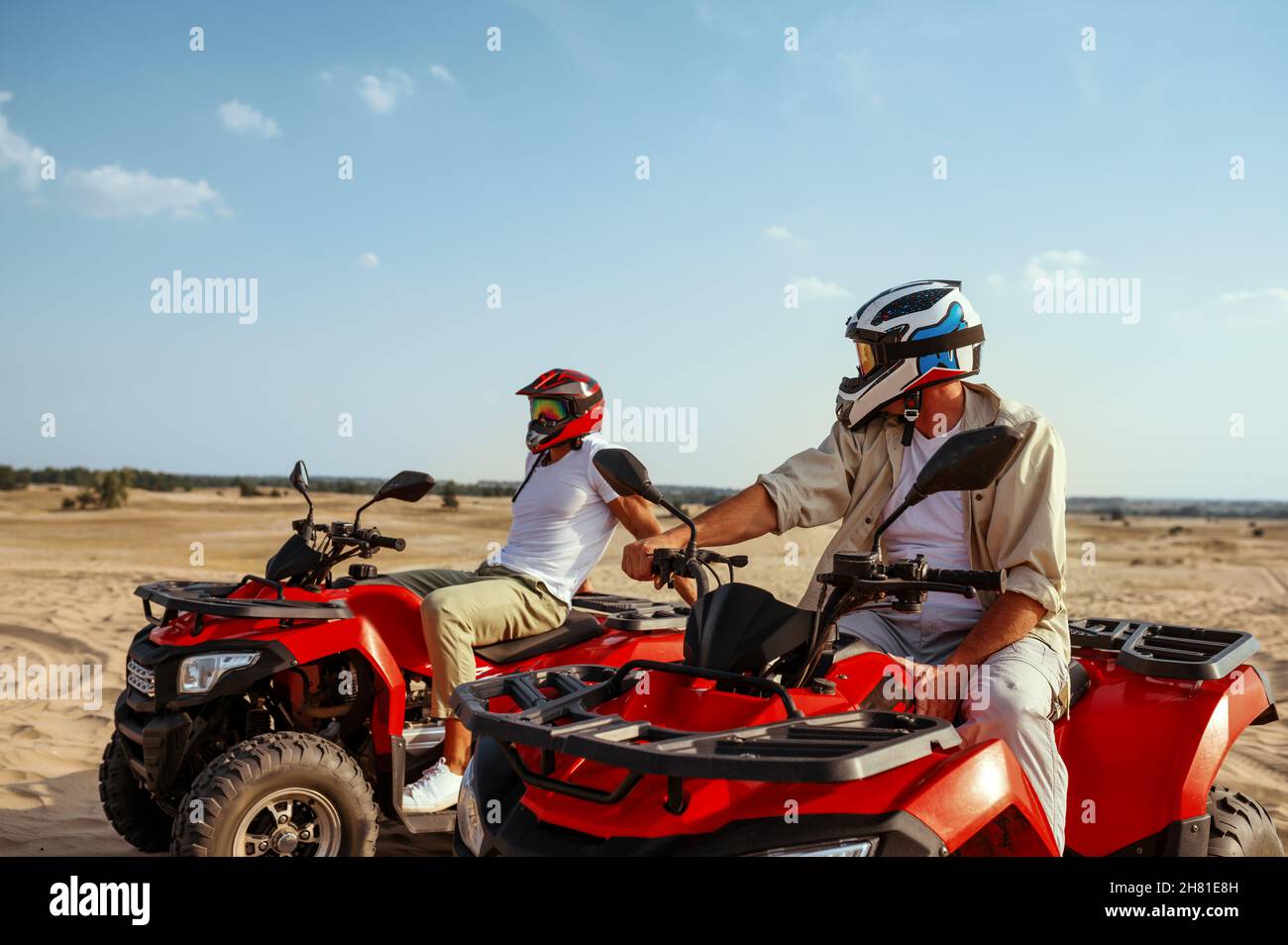 Two men in helmets ride on atv in desert Stock Photo - Alamy