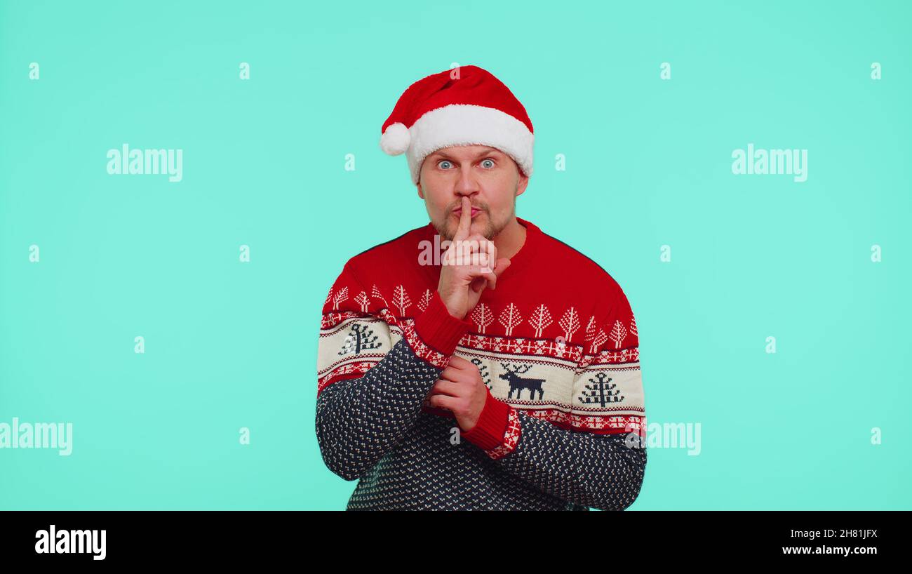 Man wears red Christmas sweater presses index finger to lips makes ...