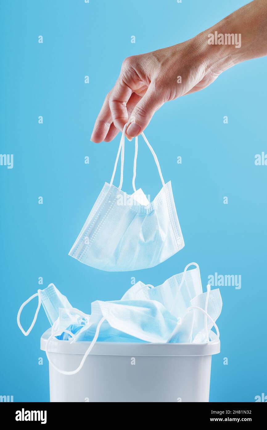 Hand throws a used face shield into the trash can on a light blue ...