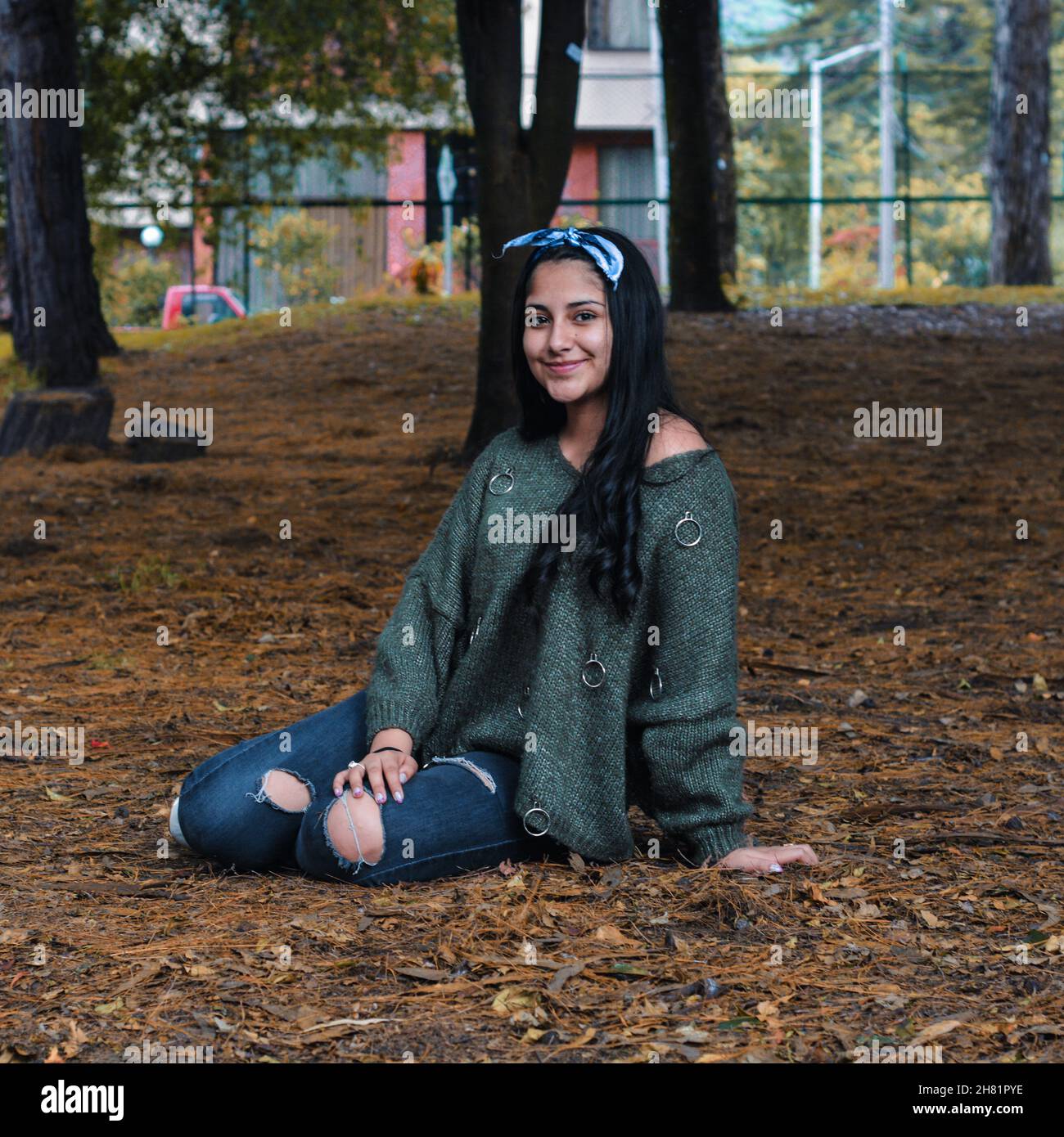 Young Colombian female wearing a green sweater and ripped jeans sitting ...