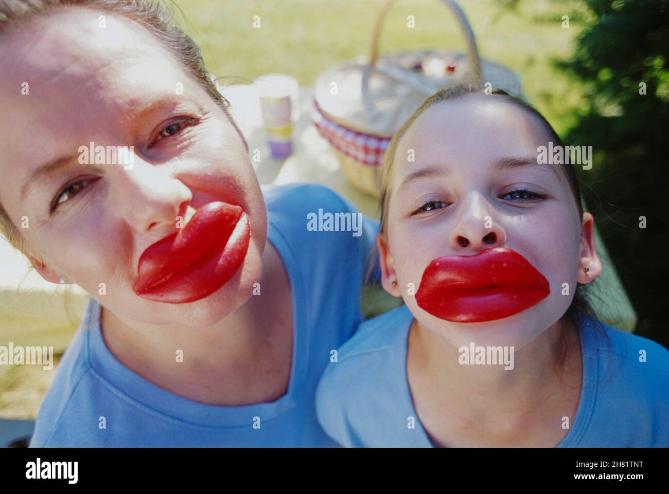Mother and daughter portrait at picnic along lake wearing red wax lips ...