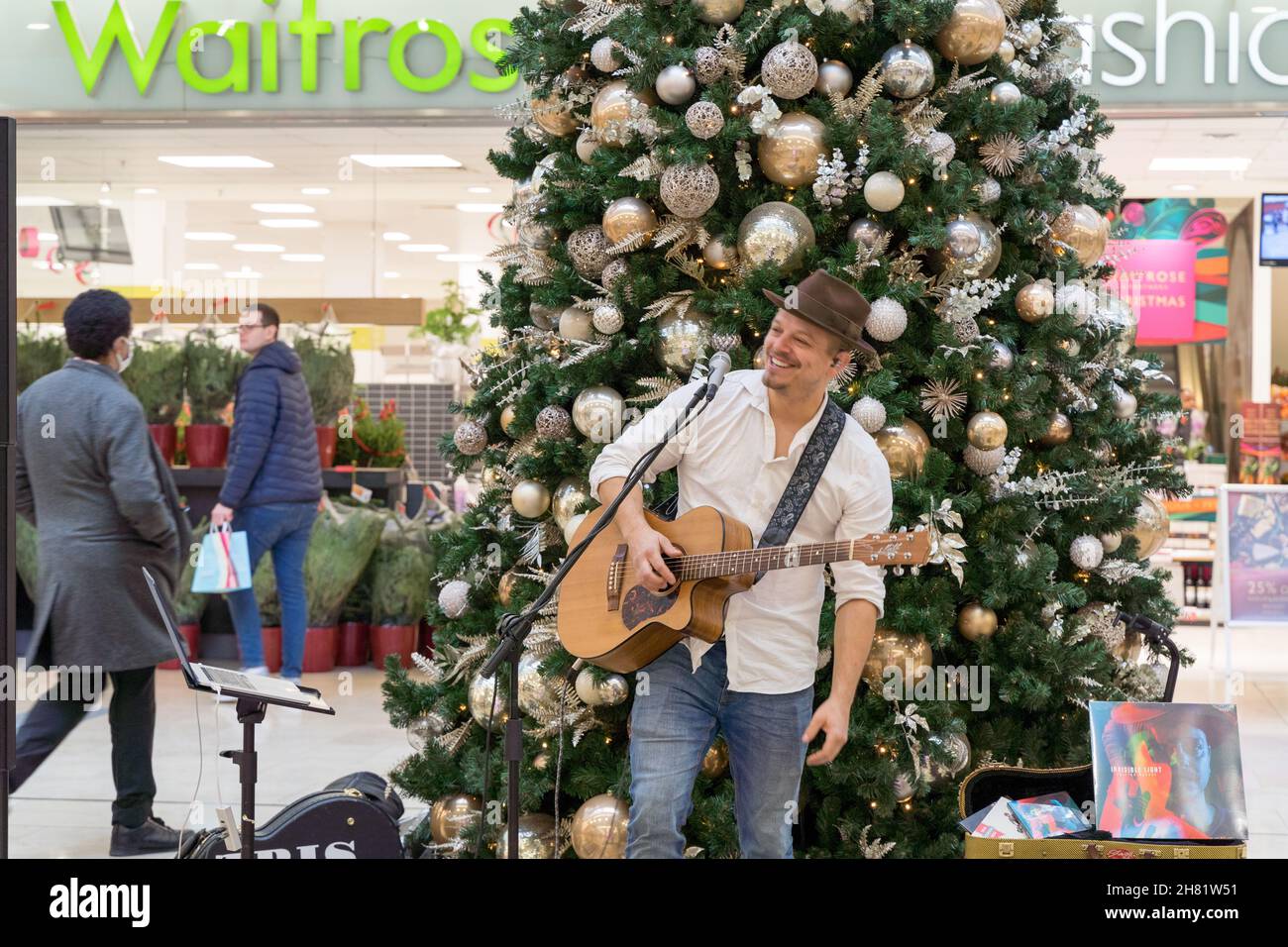 A guitarist busker playing music to shoppers in front of a Christmas ...