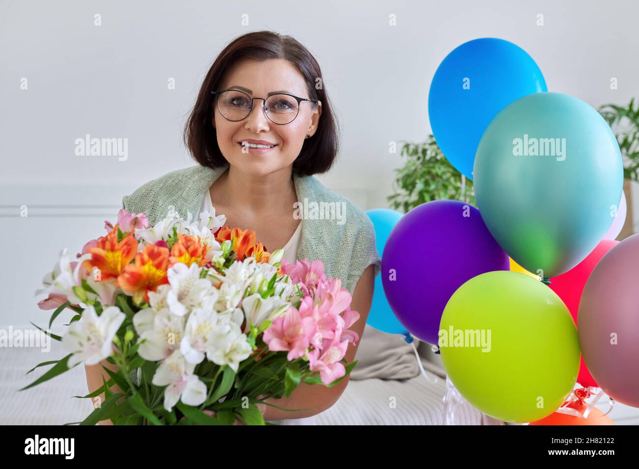 Portrait of middle aged happy woman with bouquet of flowers, balloons ...