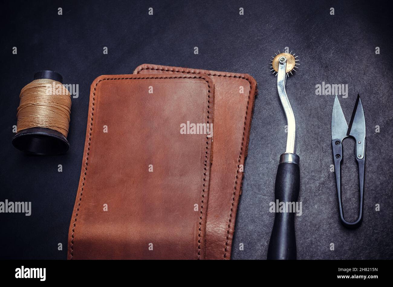 pieces of yellow leather, tools and spool of yellow thread on a black ...