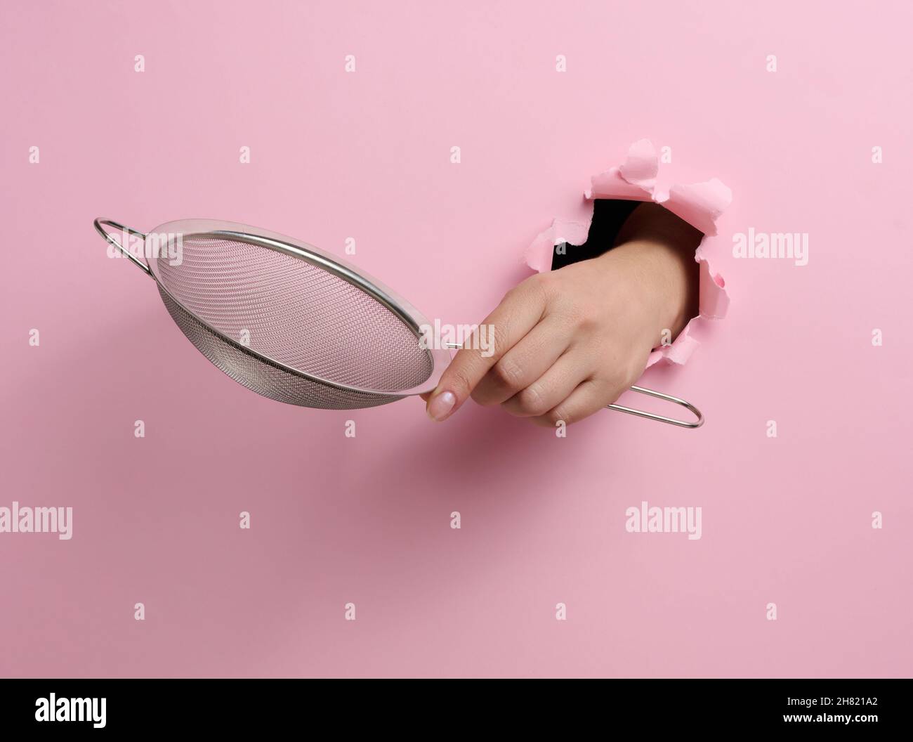 metal sieve for sifting flour in a female hand on a pink background ...