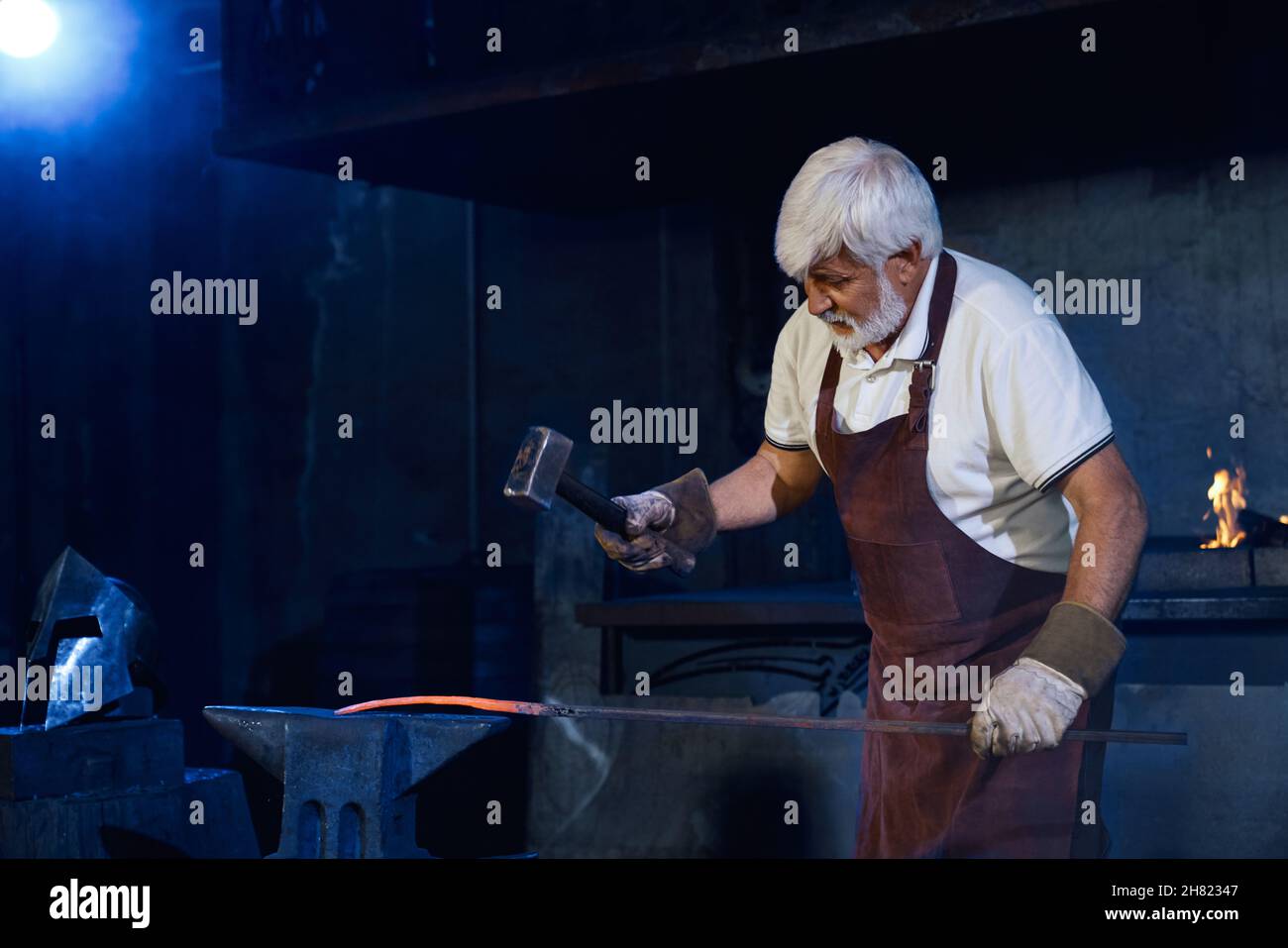 Professional blacksmith with grey beard and hair beating molten steel ...
