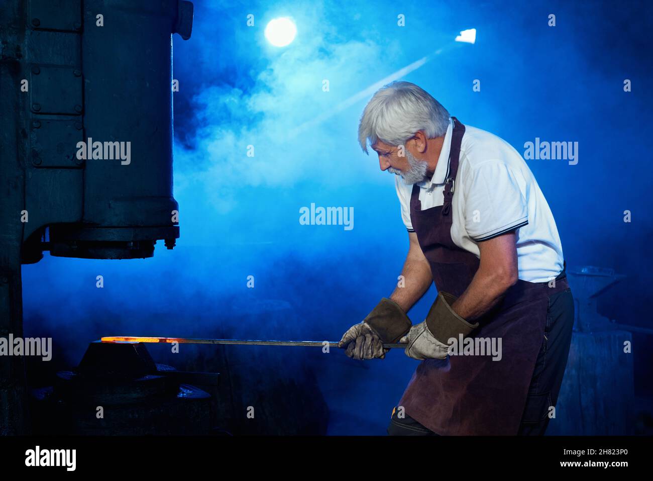 Side view of caucasian grey haired blacksmith in protective uniform ...