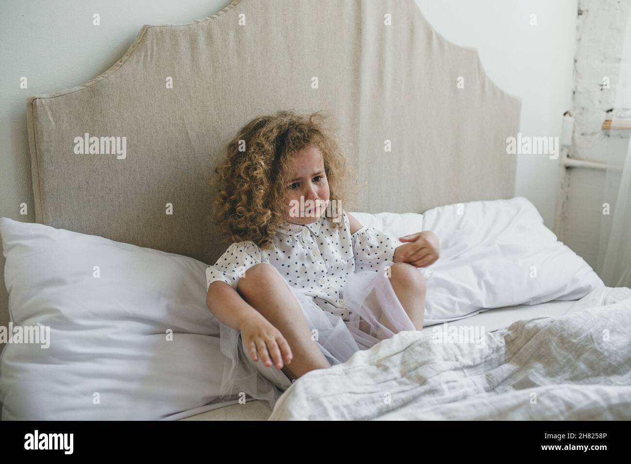 a little girl with beautiful curly hair is crying sitting in bed. upset ...