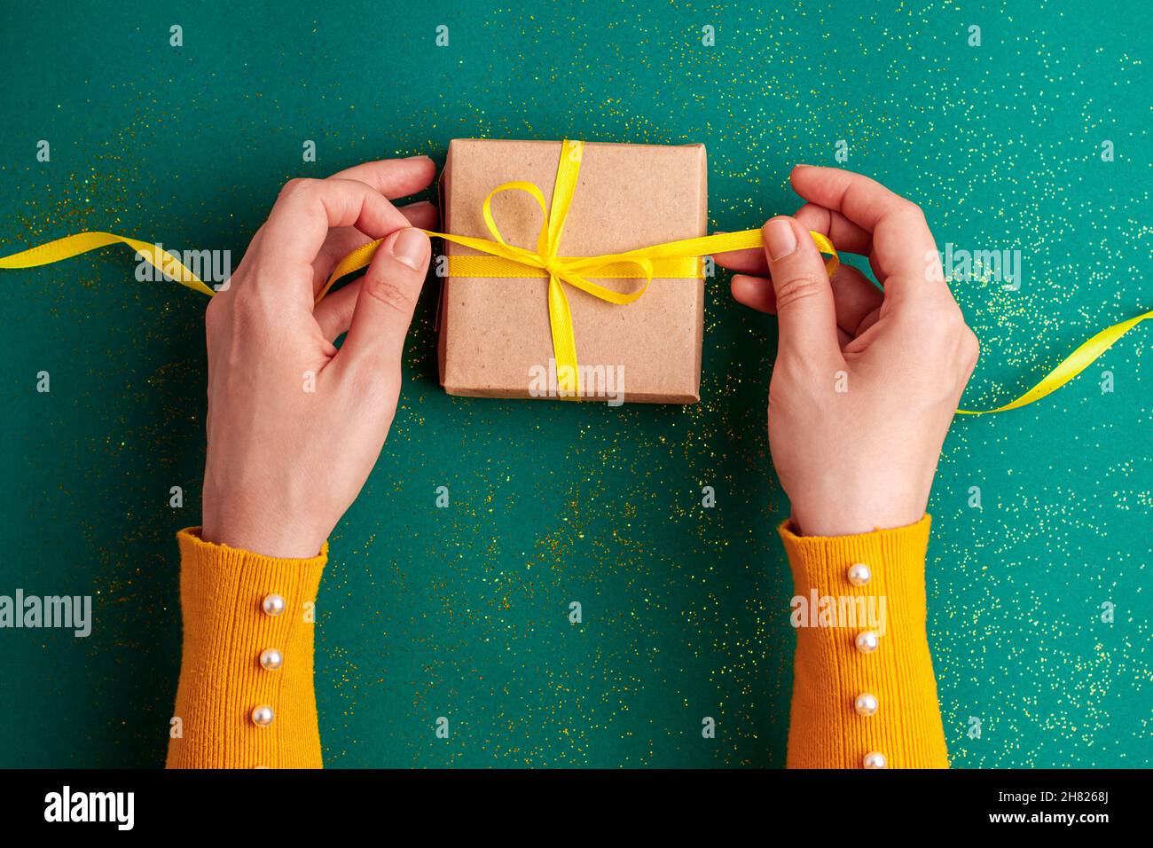 Human hands untied brown gift box with a yellow satin ribbon bow on ...