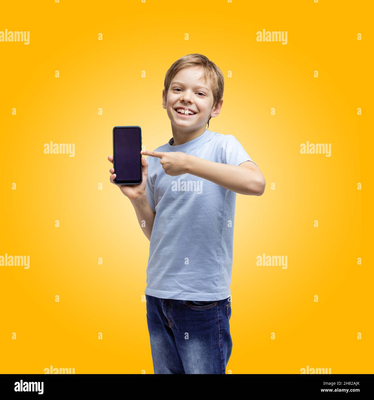 Cute young boy holding and pointing at smart phone, over yellow ...