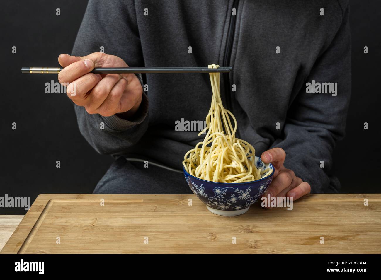 holding spaghetti with chopsticks and pulling them out of a blue bowl ...