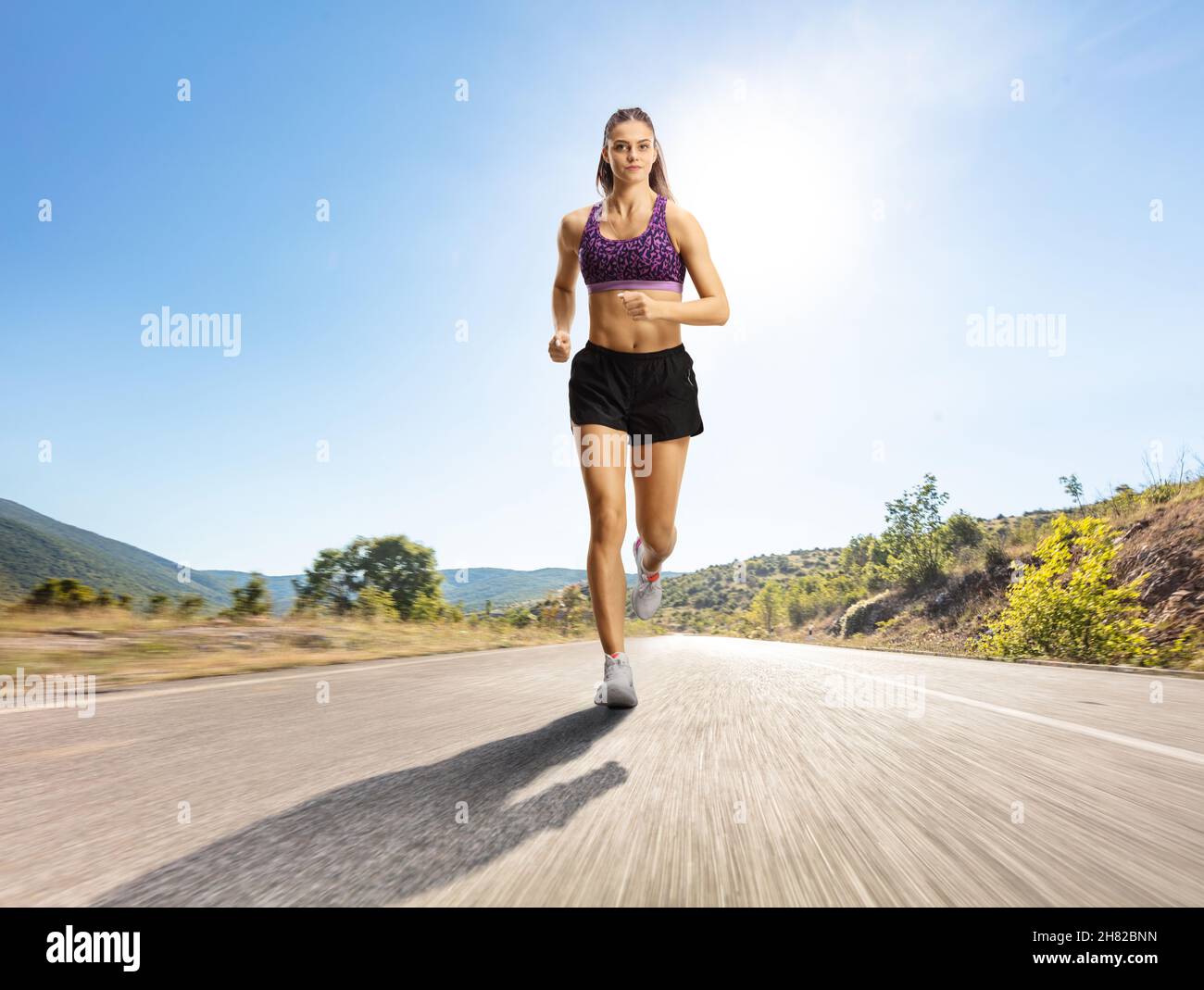 Young female wearing crop top and shorts and running on an open road ...