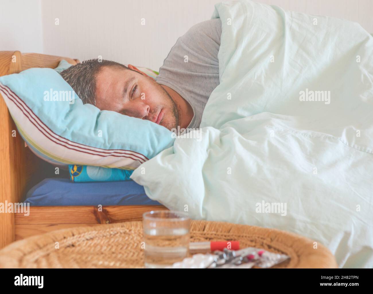 Sick man sleeping in a bed, pills and water glass in the foreground ...