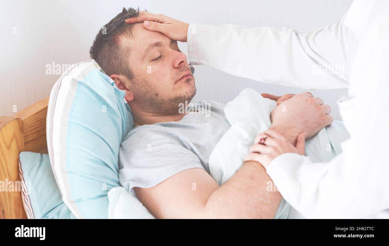 Doctor checking fever temperature of senior man lying on bed. Man ...