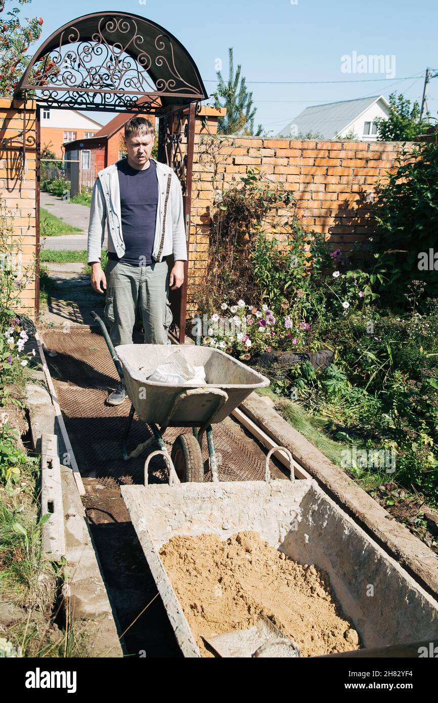 A man unloads sand into a cement mixture for pouring a garden path ...