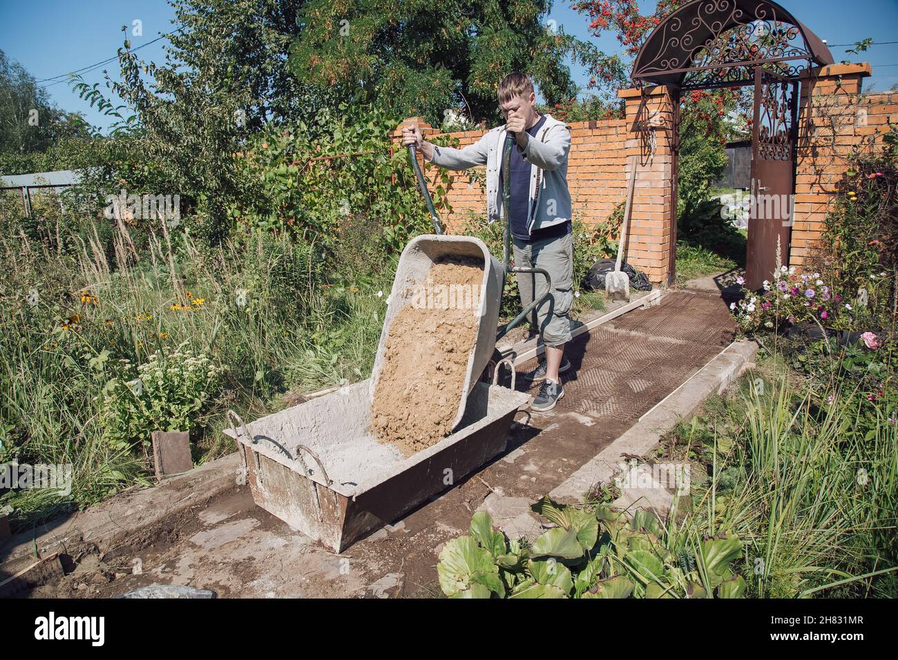 A man unloads sand into a cement mixture for pouring a garden path ...