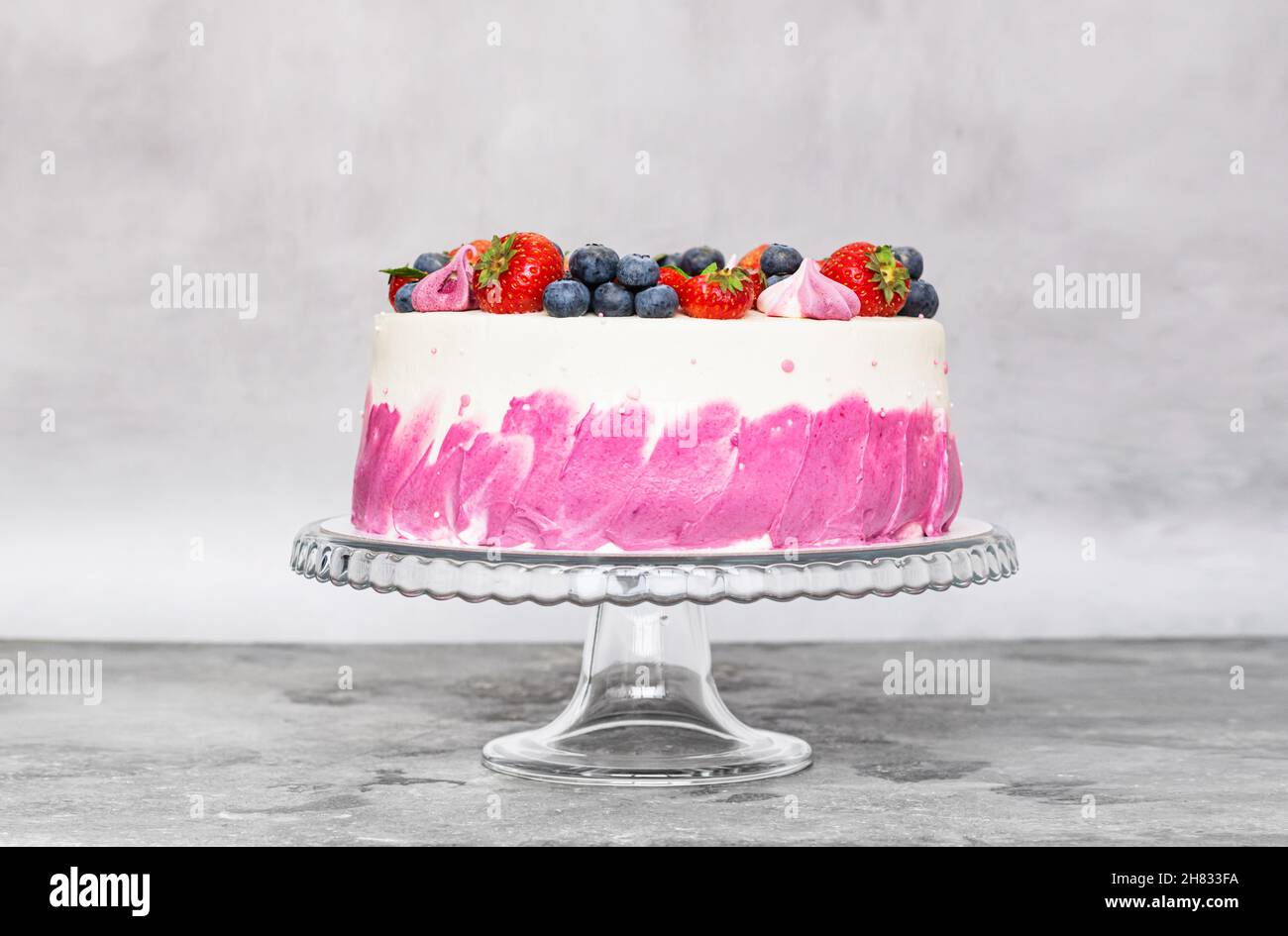 Delicate cake garnished with fresh strawberries blueberries on a gray ...