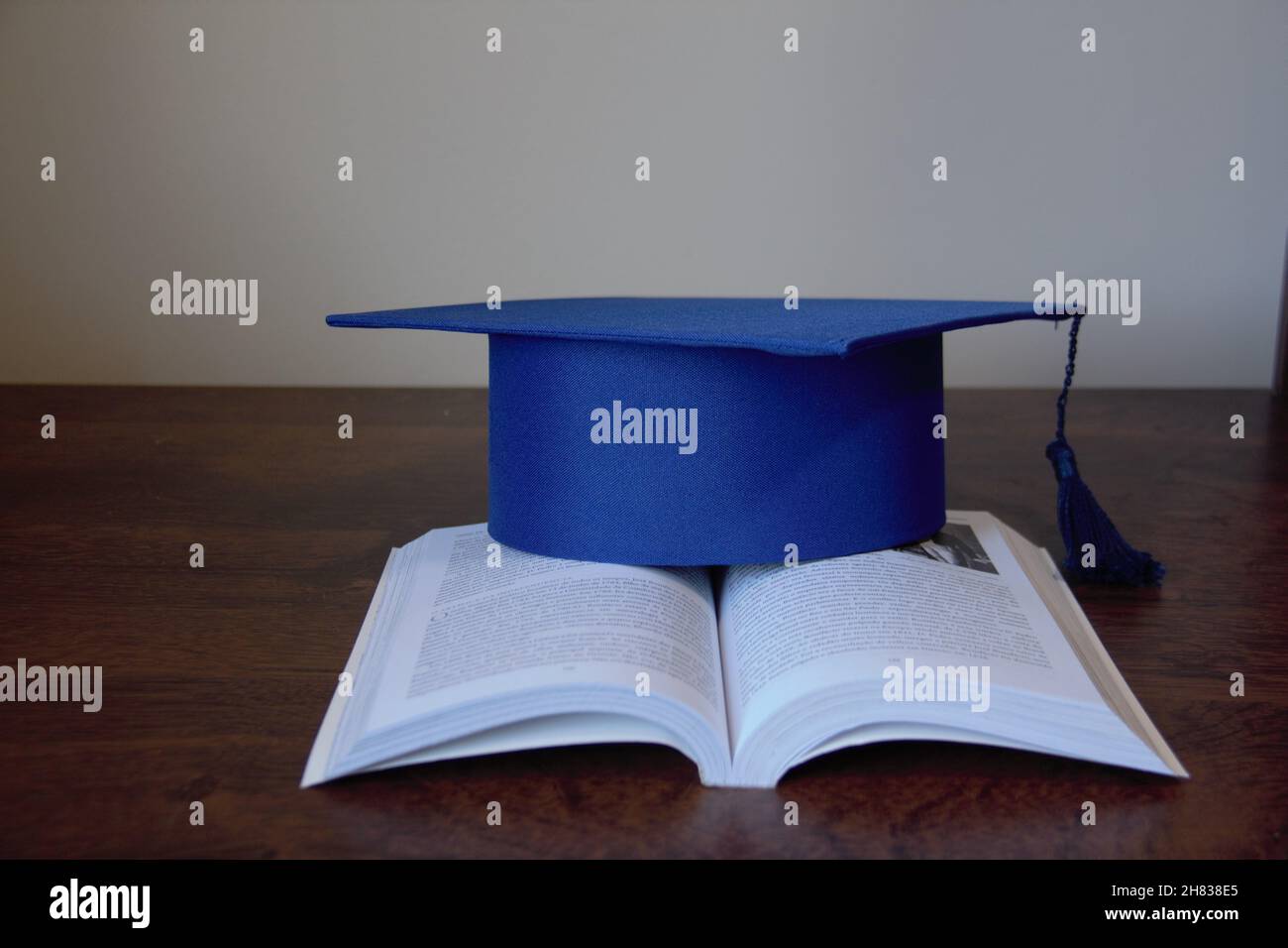 Graduation cap, isolated, on an open book on a wooden table with white ...